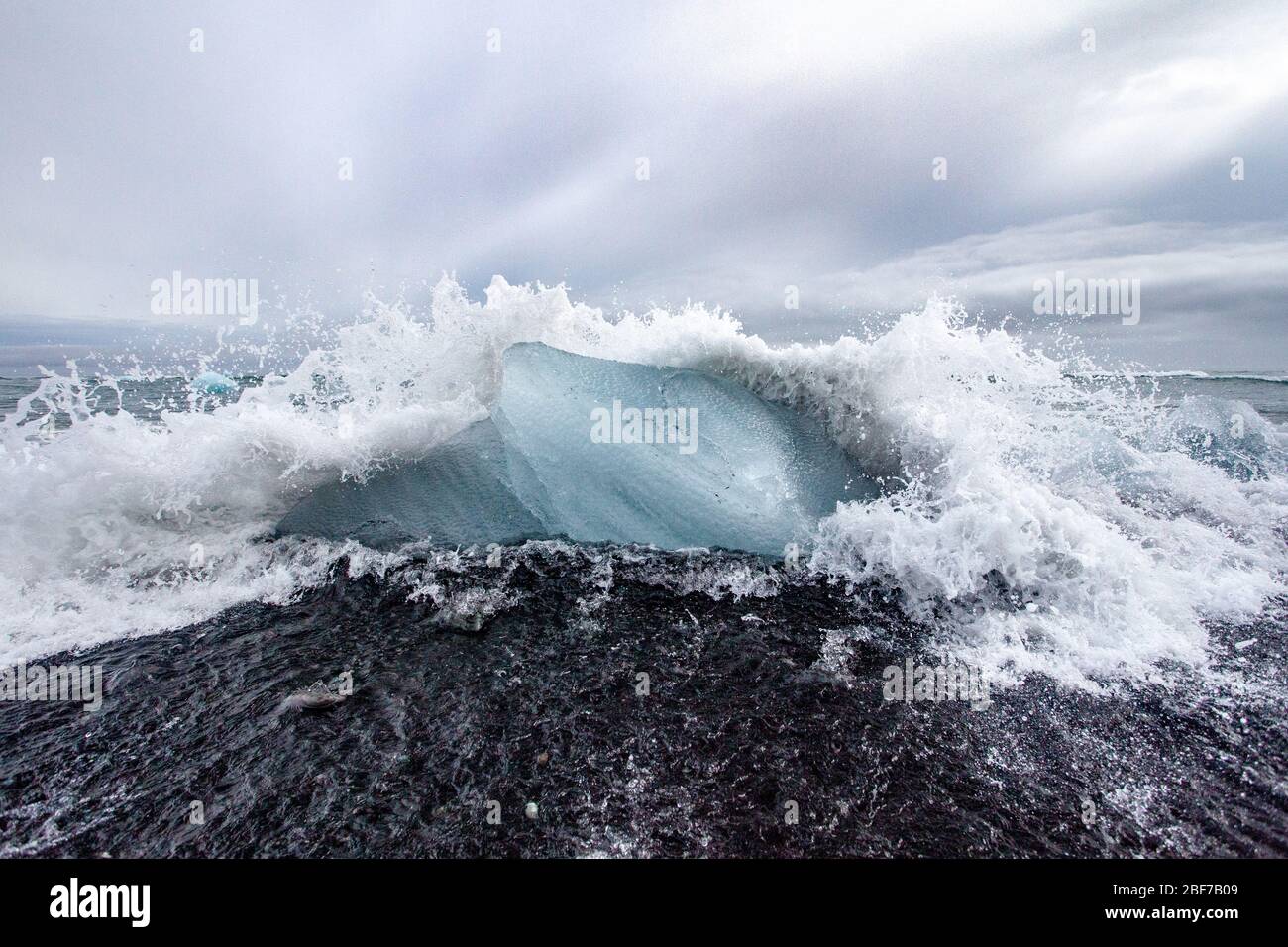 A wave crashes over a large chunk of glacial ice on the shores of ...