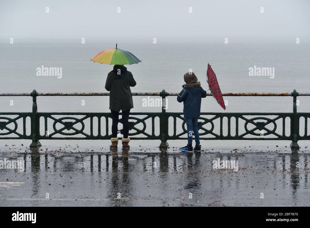 A parent and child with umbrellas on a rainy spring day on Brighton and ...
