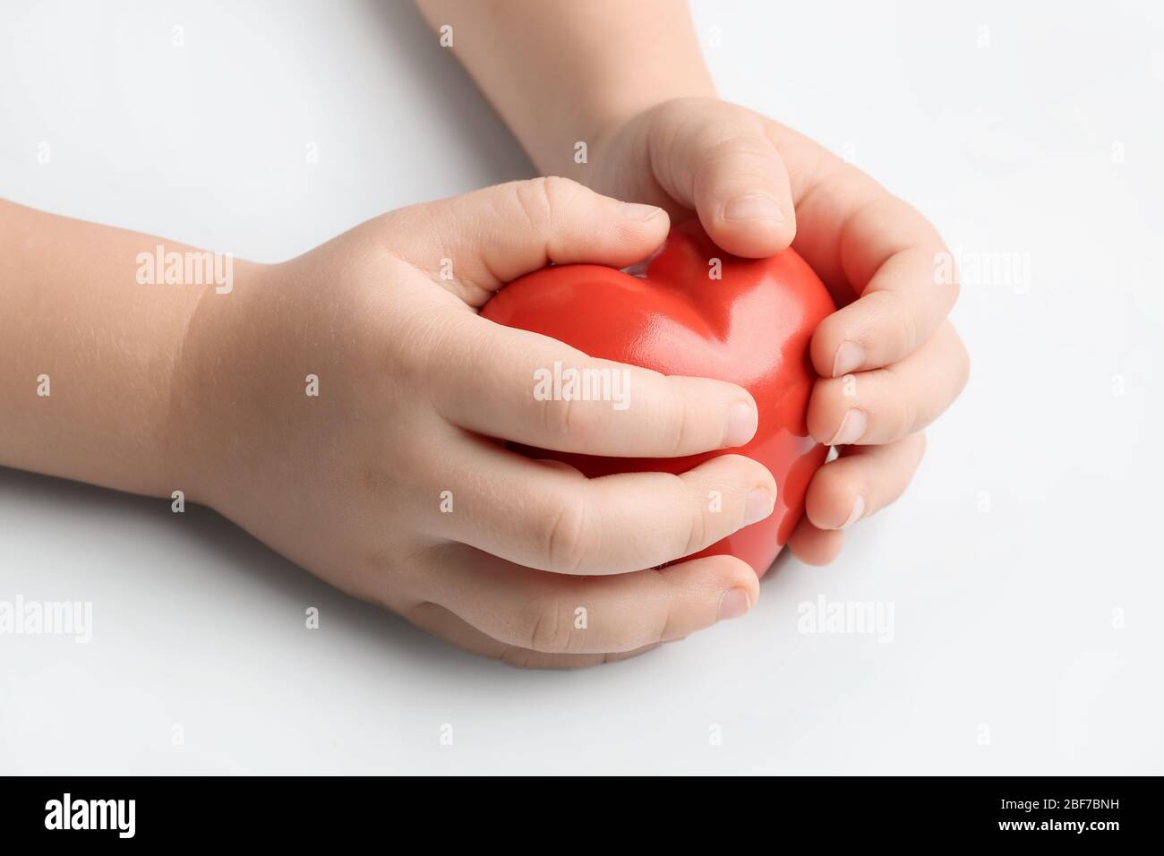 Child's hands with red heart on white background. Cardiology concept ...