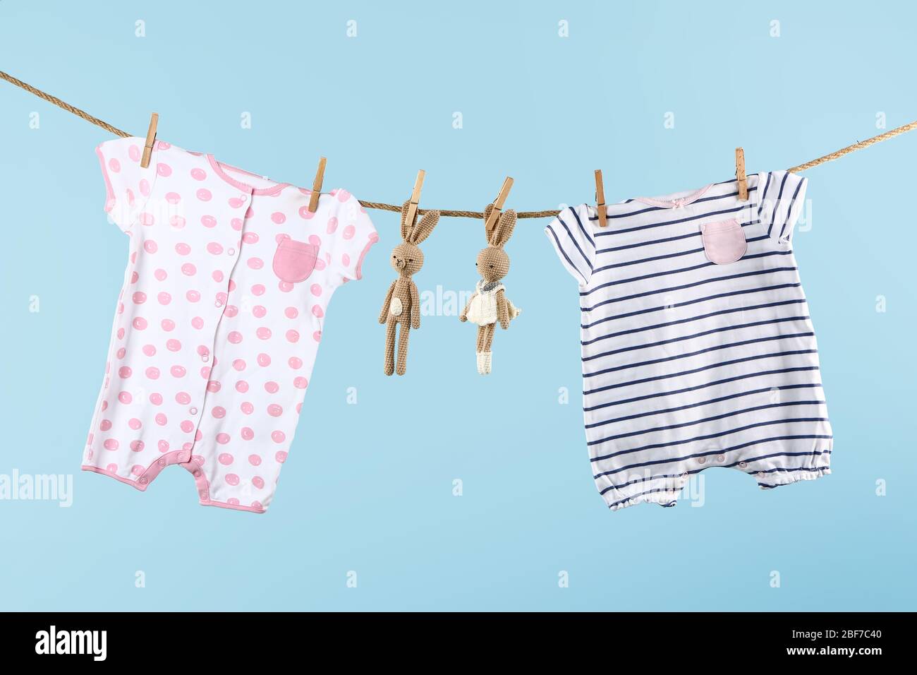 Baby clothes with toys hanging on rope against color background Stock ...