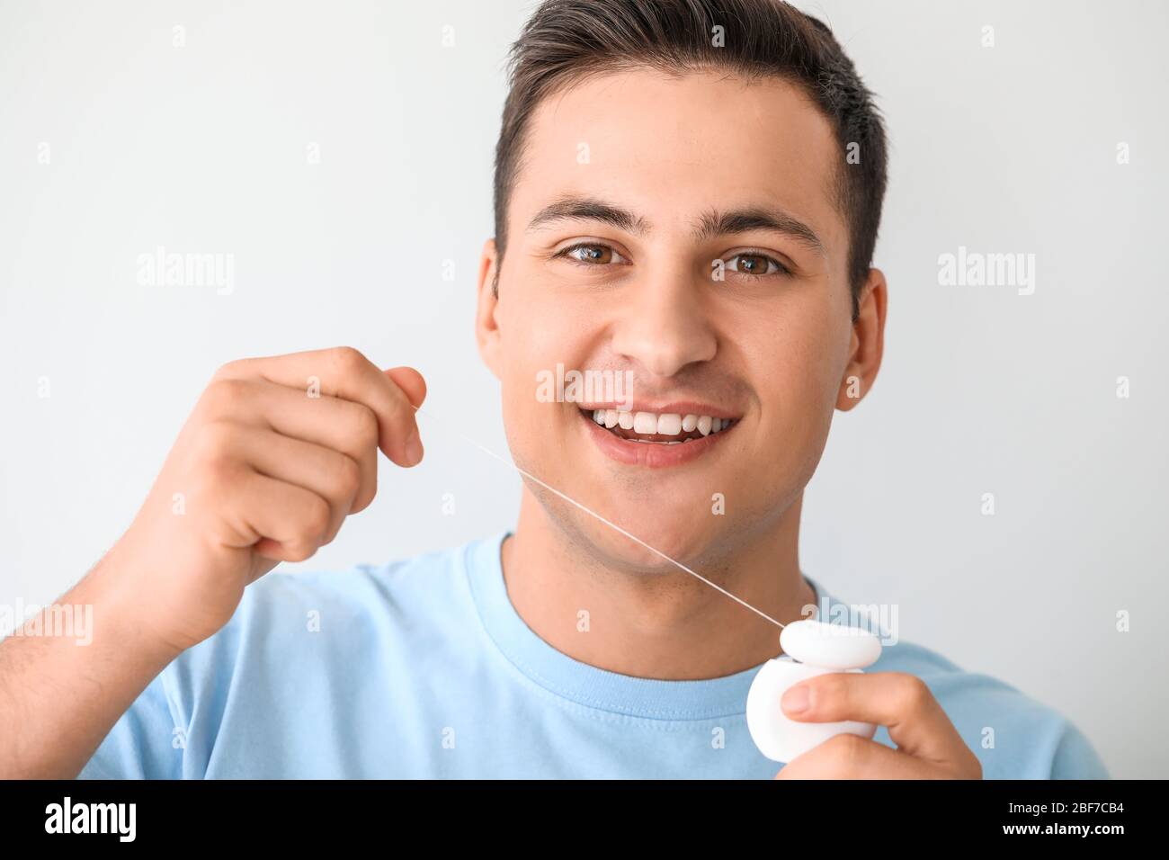 Handsome man flossing teeth on light background Stock Photo - Alamy