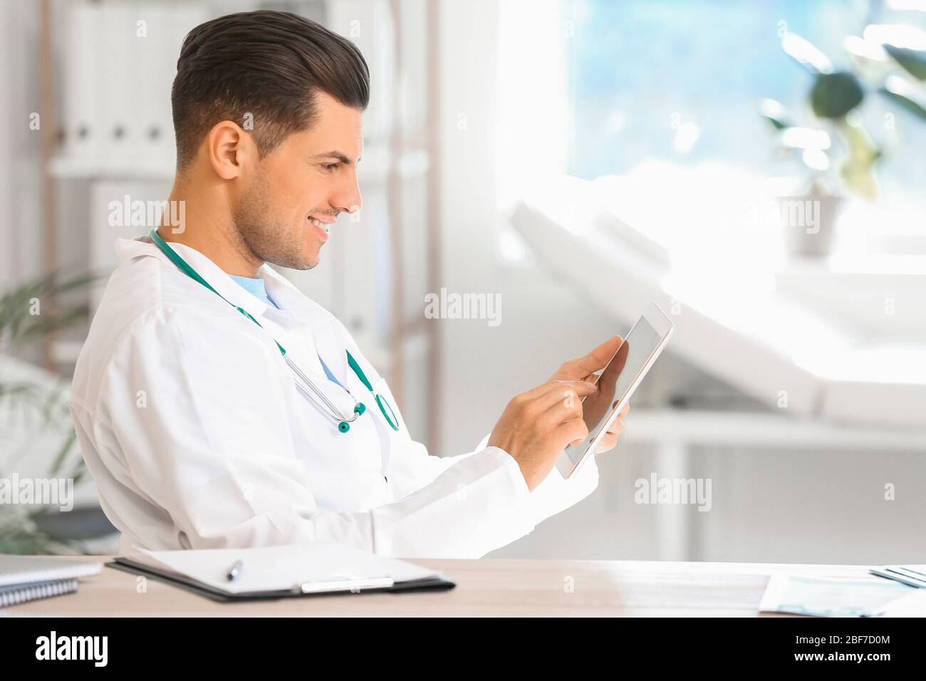 Young male doctor with tablet computer working in clinic Stock Photo ...