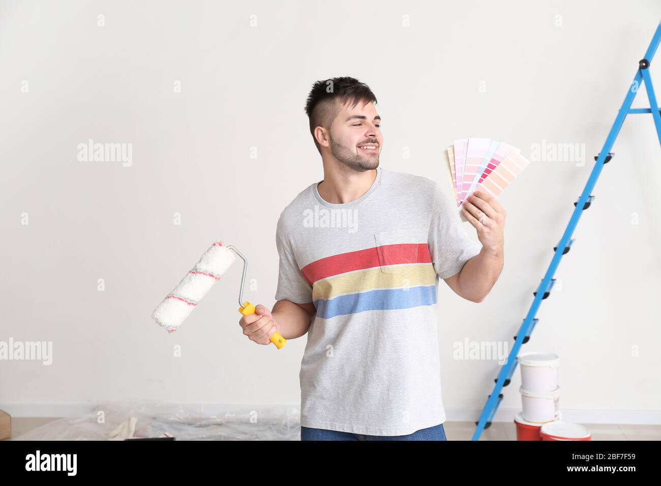 Young man with color swatches and paint roller indoors Stock Photo - Alamy