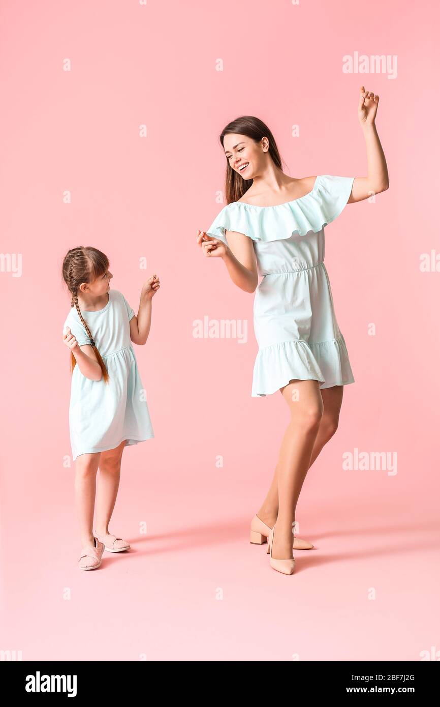 Happy mother and her little daughter dancing against color background ...