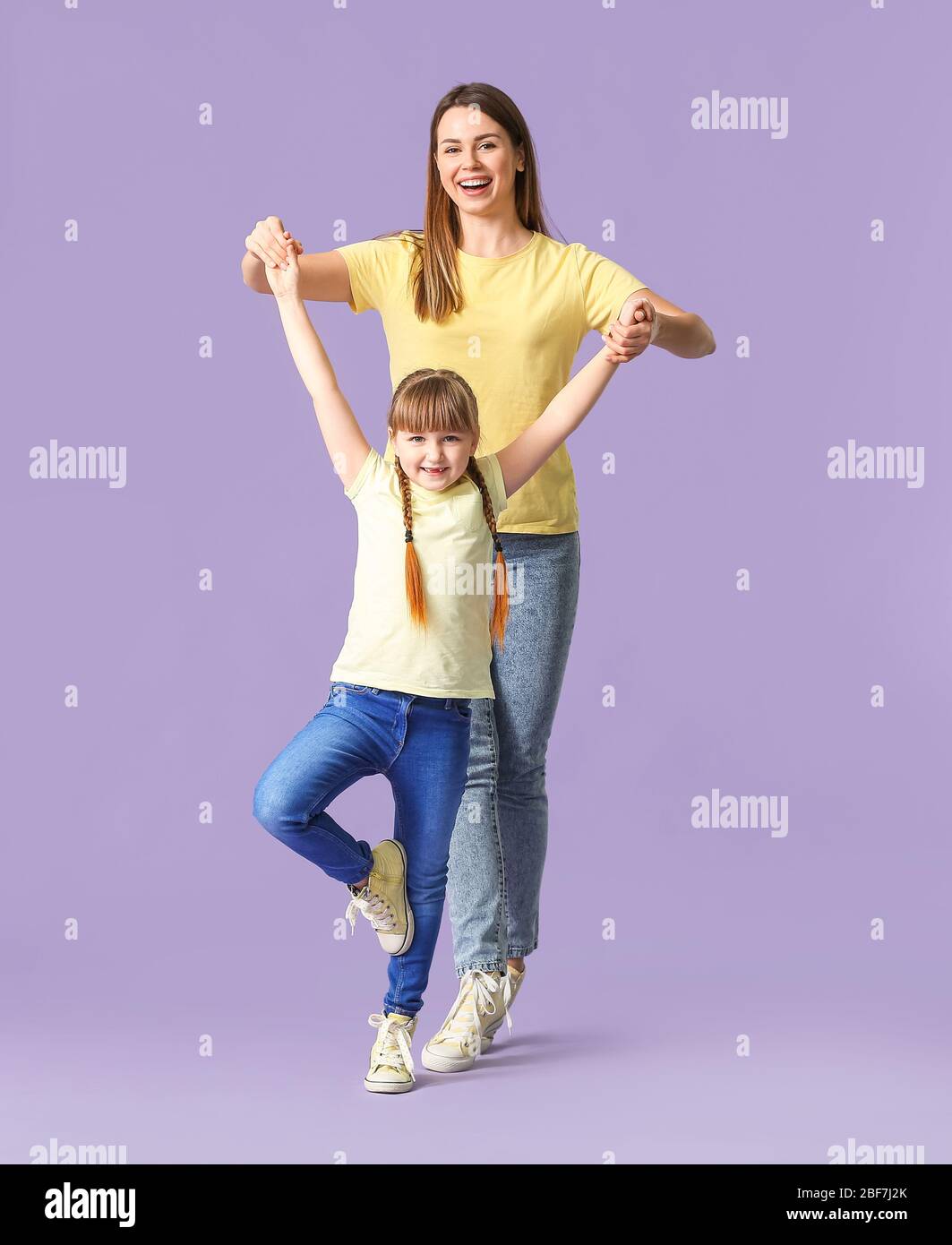 Happy mother and her little daughter dancing against color background ...