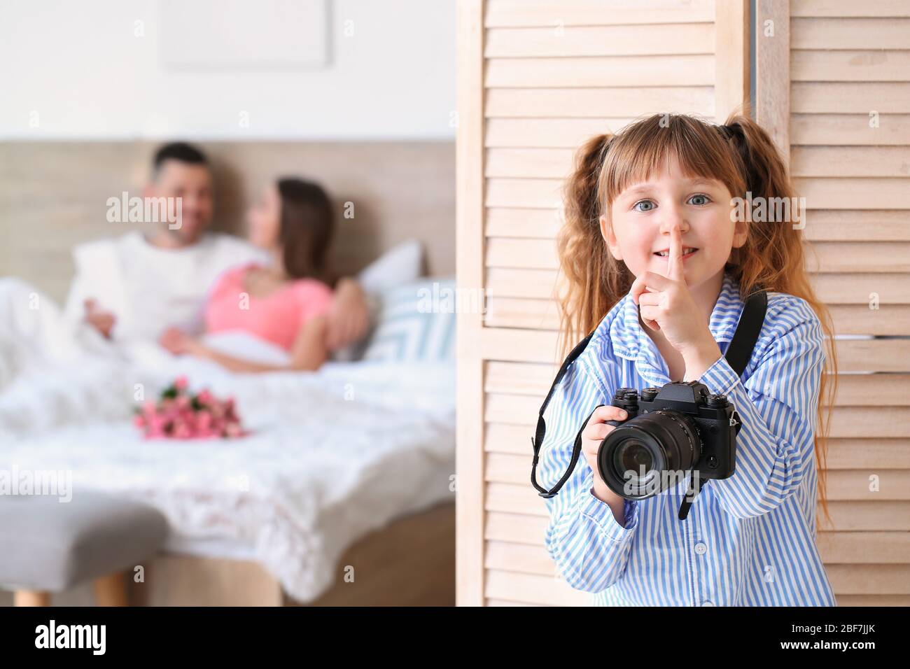 Little girl with photo camera hiding behind folding screen in bedroom ...