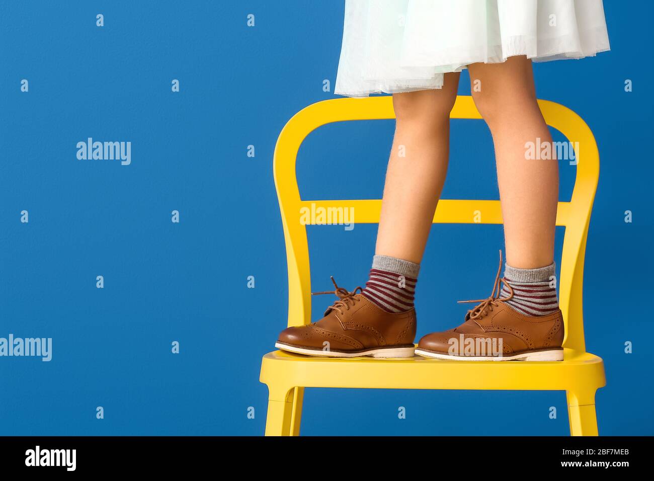 Little girl standing on chair against color background Stock Photo - Alamy