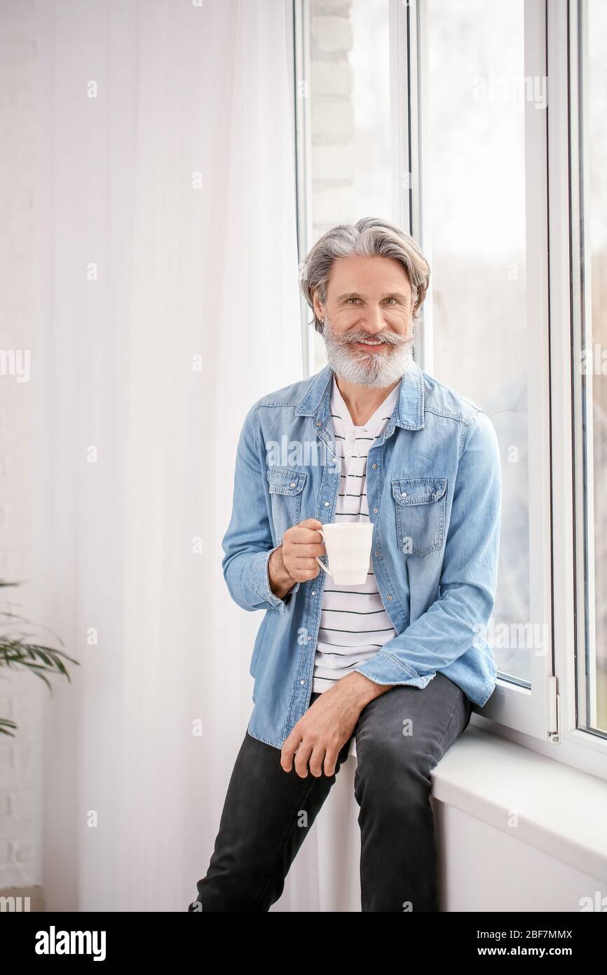 Stylish elderly man drinking tea near window at home Stock Photo - Alamy