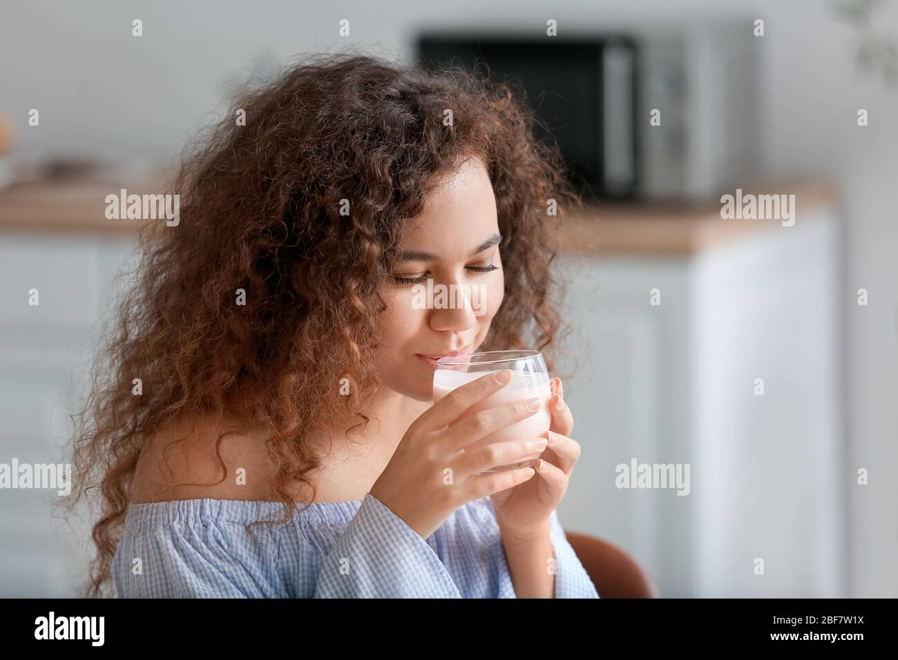 Young woman drinking tasty yogurt in kitchen Stock Photo - Alamy