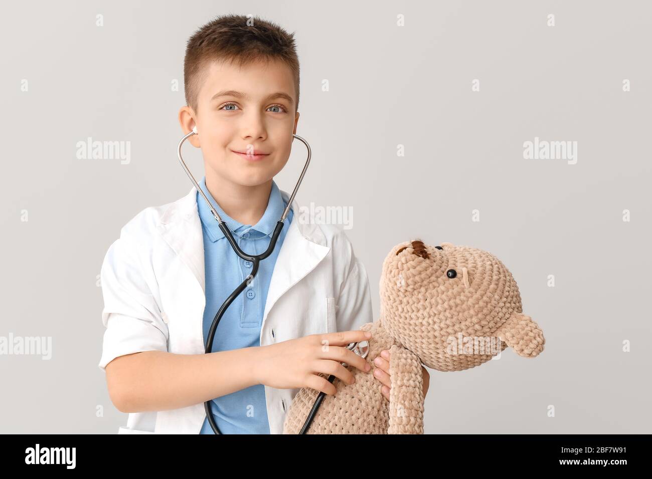 Cute little doctor with teddy bear on grey background Stock Photo - Alamy