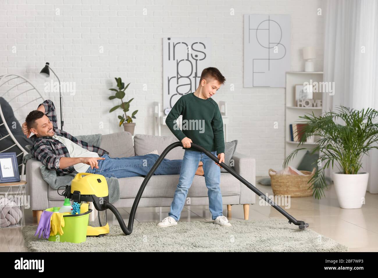 Little boy hoovering floor and his lazy father relaxing on sofa Stock ...