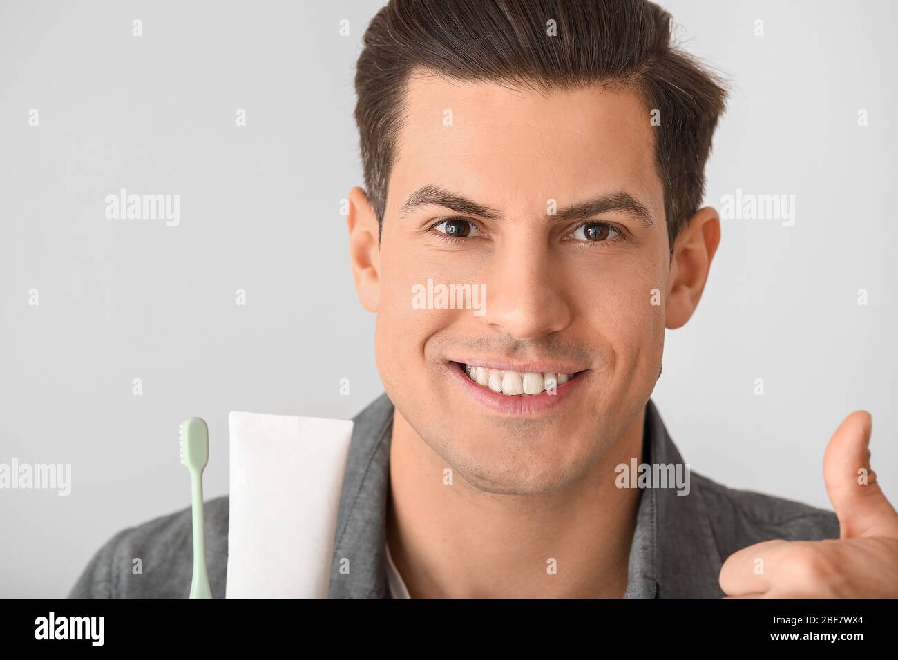 Young man with tooth brush and paste showing thumb-up on light ...