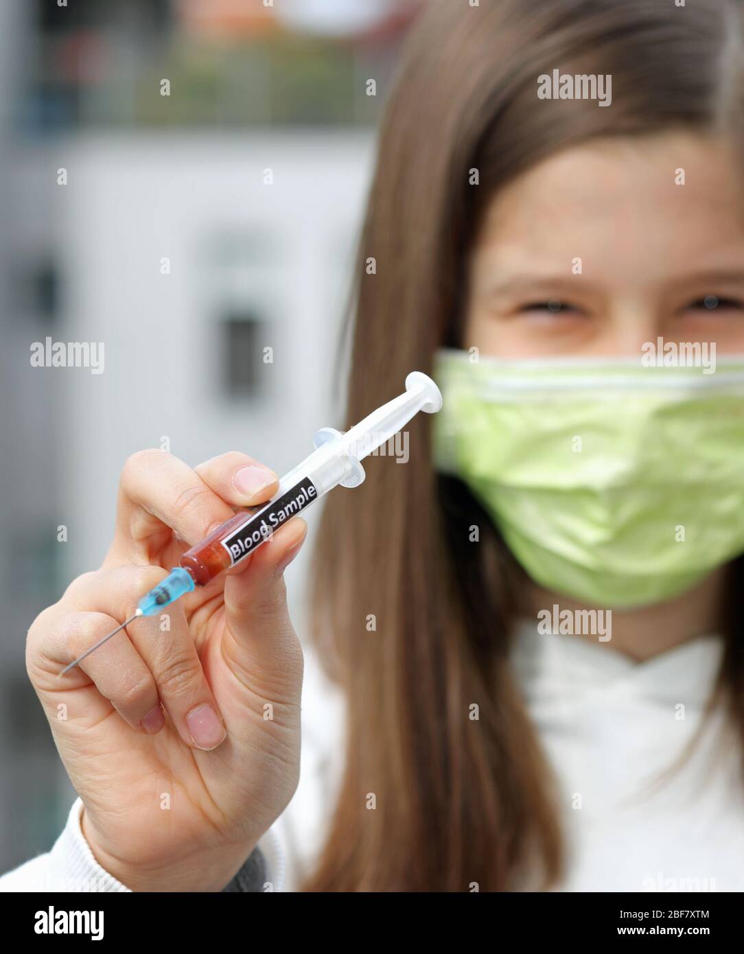hand of young nurse wears surgical mask with syringe containing blood ...
