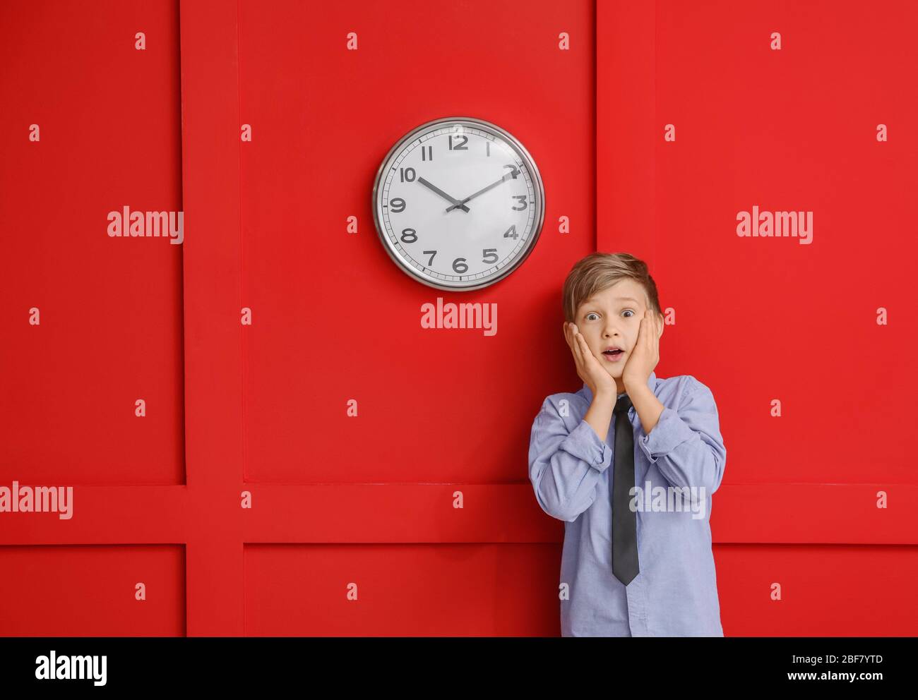Shocked little boy near color wall with clock Stock Photo - Alamy