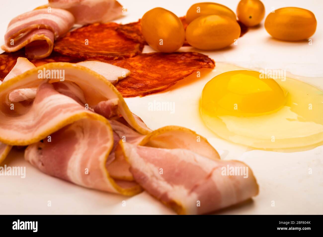 A broken chicken egg without a shell, slices of sausage and bacon and ...