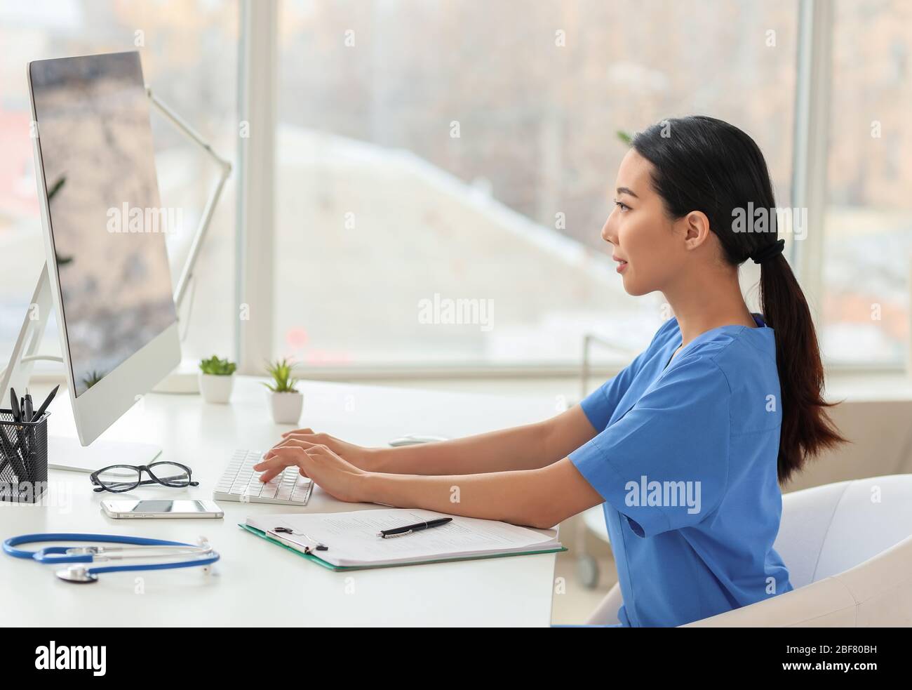 Female Asian doctor working on computer in clinic Stock Photo - Alamy