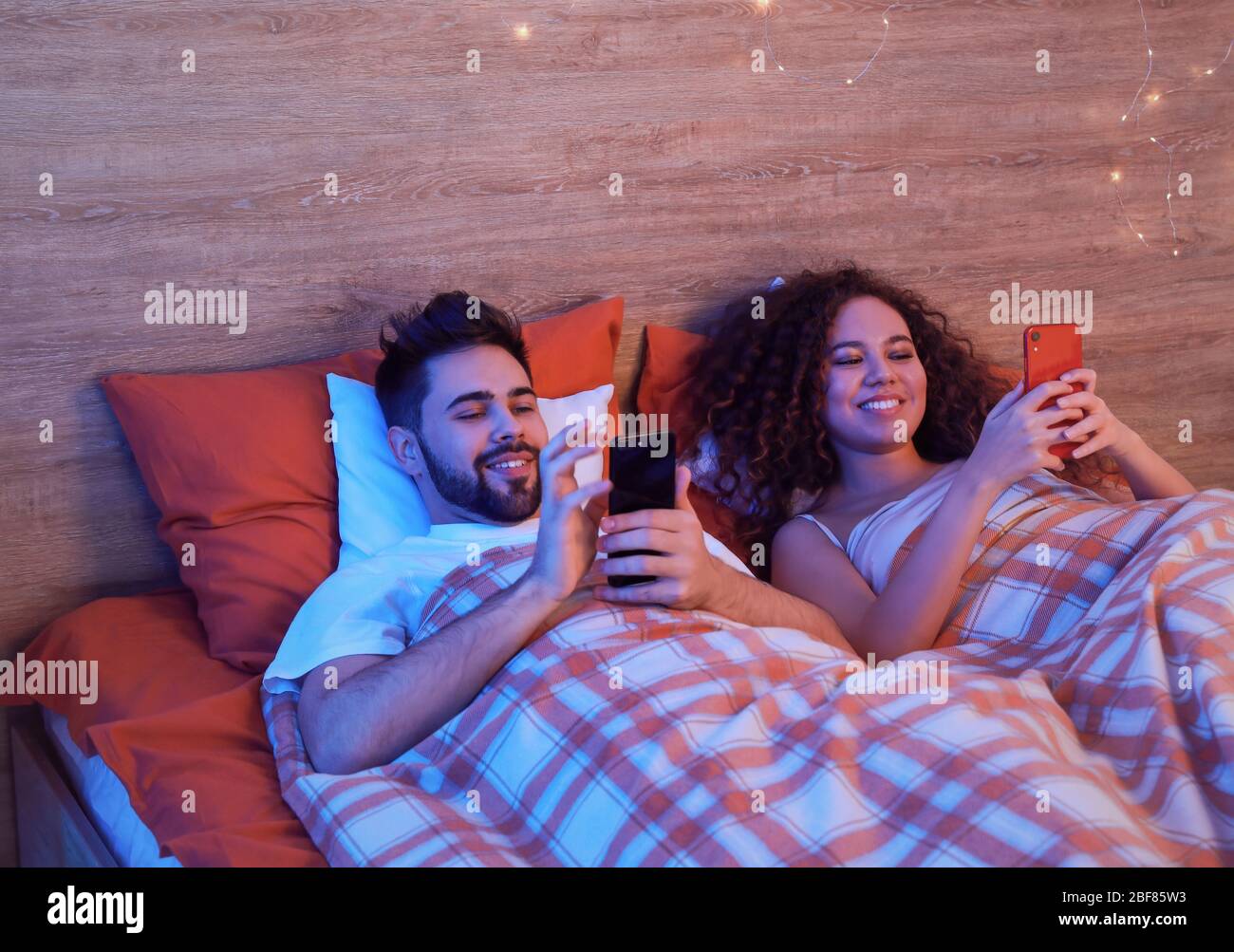 Happy young couple with mobile phones in bedroom Stock Photo - Alamy