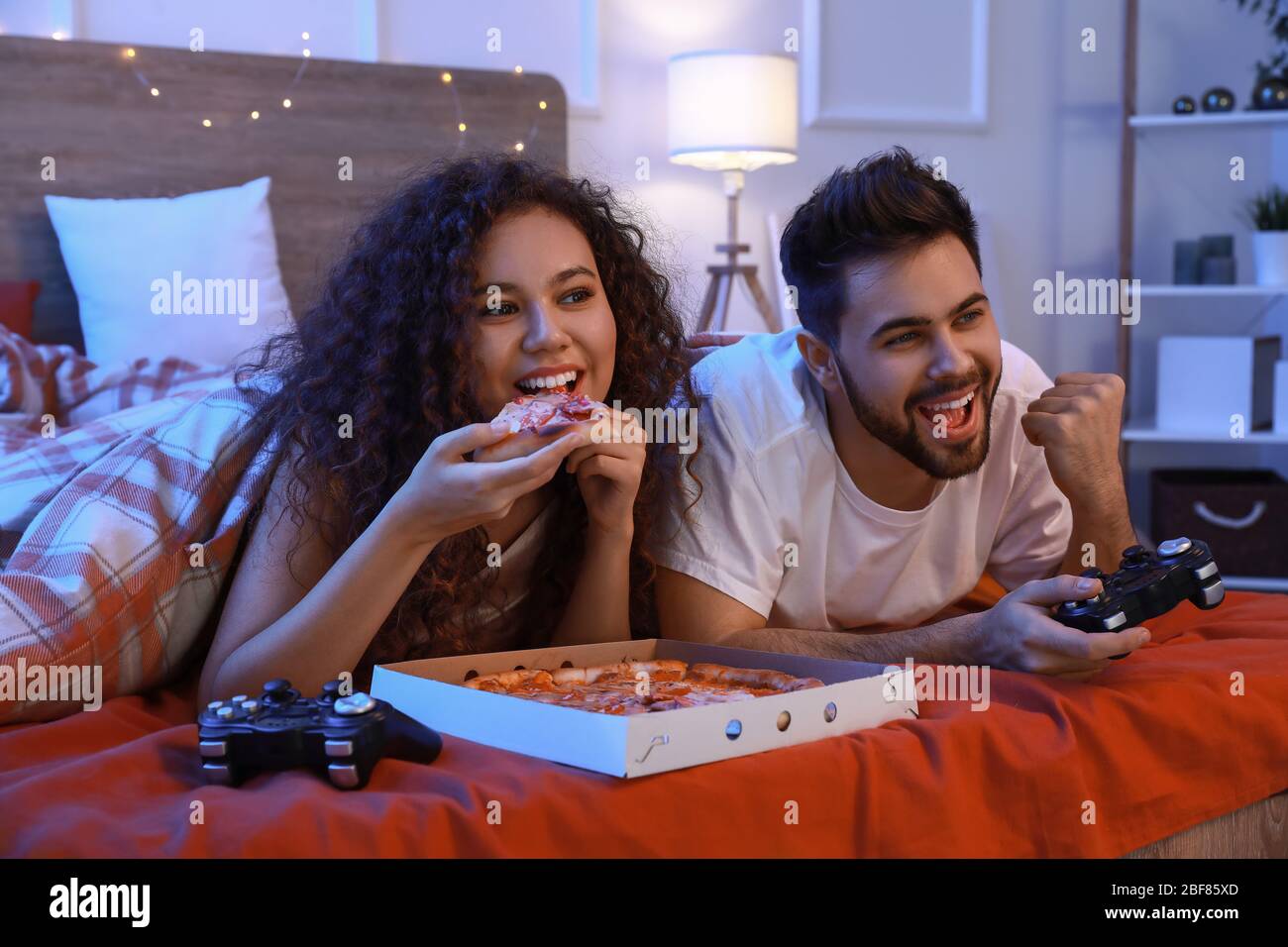 Happy young couple playing video games in bedroom Stock Photo - Alamy