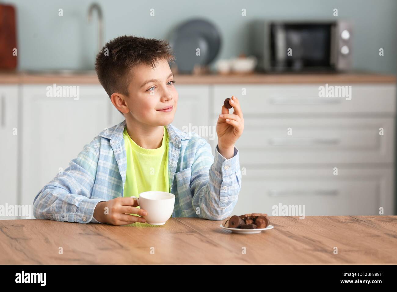 Cute little boy eating chocolate candies in kitchen Stock Photo - Alamy