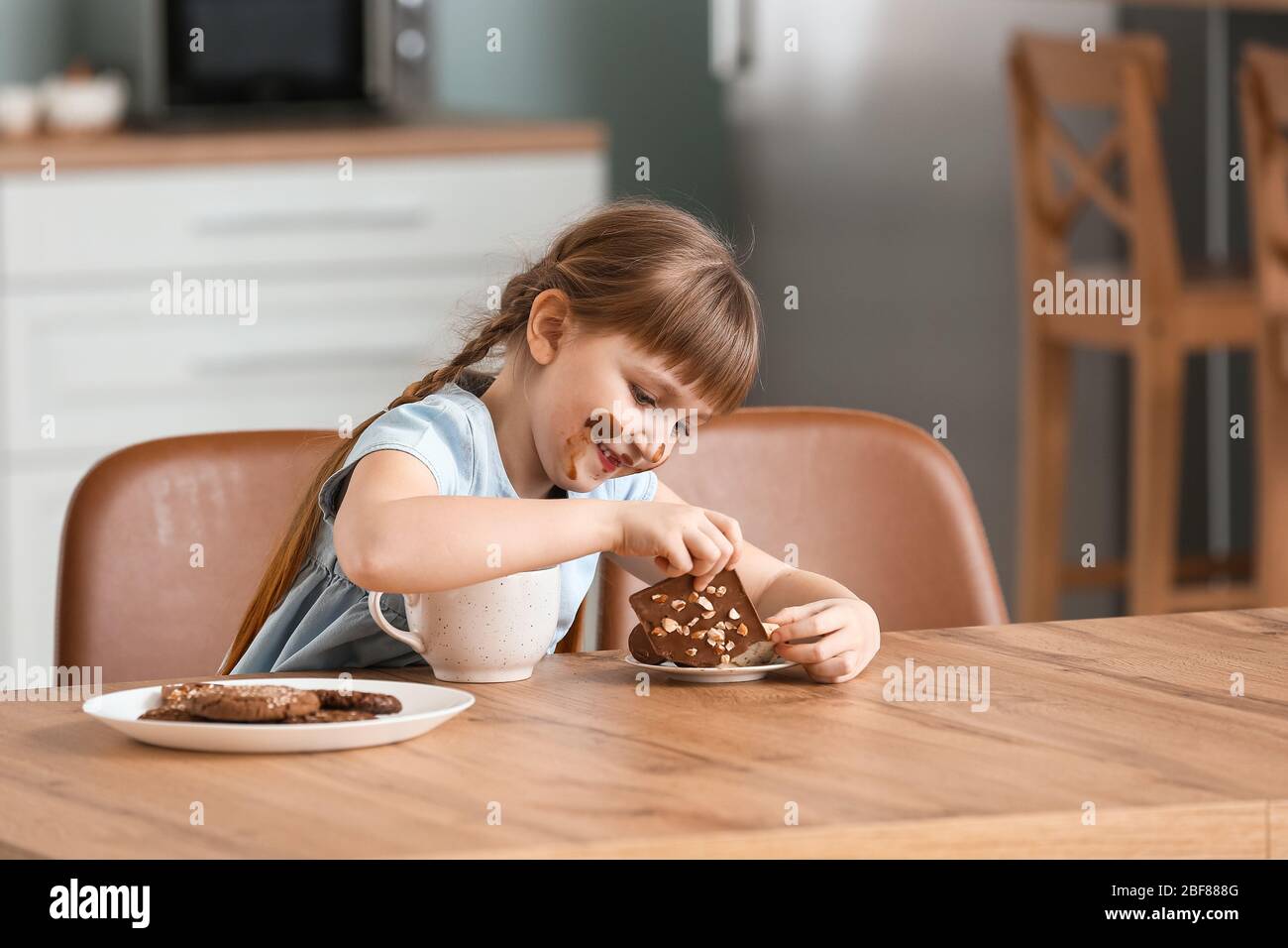 Cute little girl eating chocolate in kitchen Stock Photo - Alamy