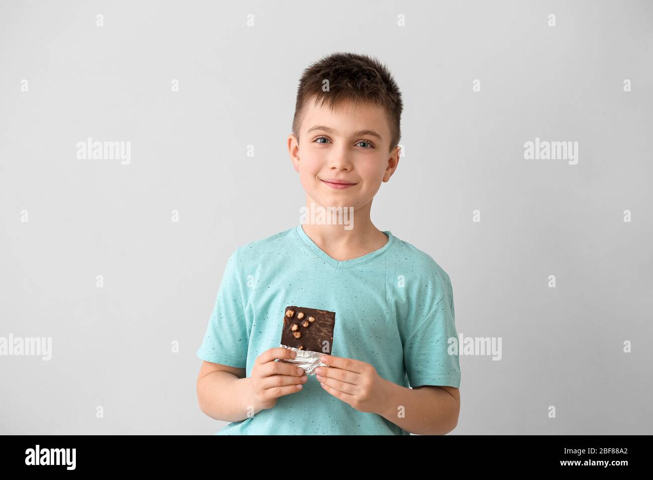 Cute little boy eating chocolate on light background Stock Photo - Alamy