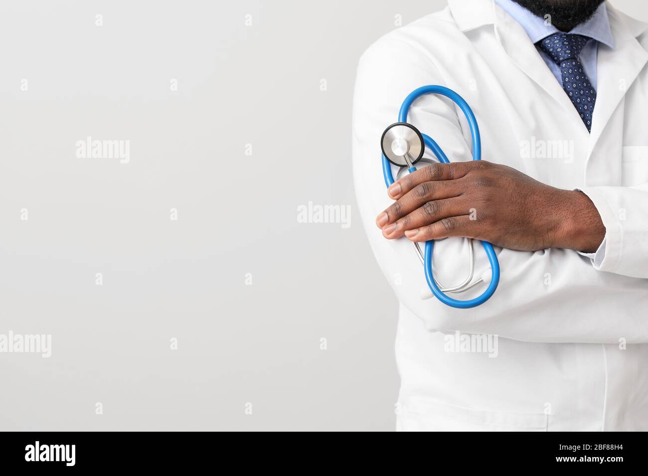 African-American doctor with stethoscope on light background, closeup ...