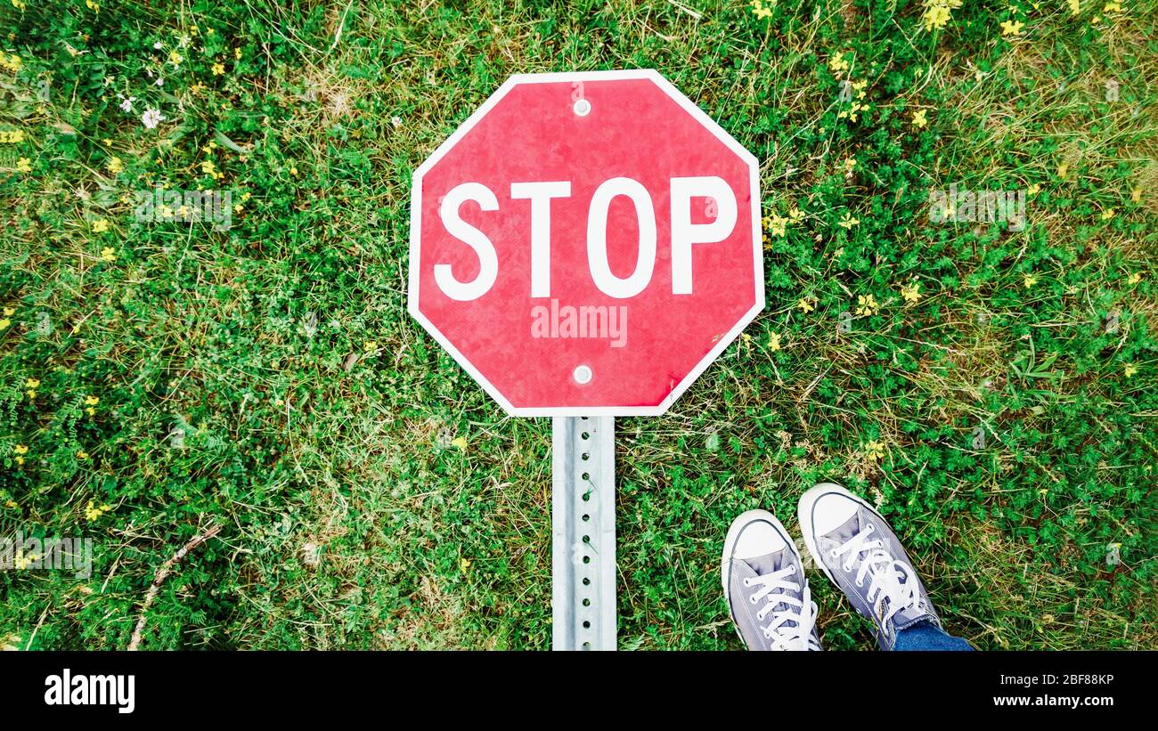 Feet and red stop sign on the green grass background. Prohibition ...