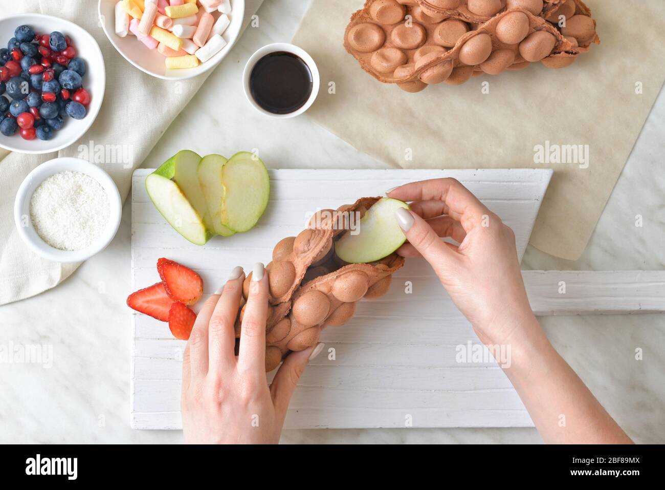 Woman preparing sweet bubble waffles at table, top view Stock Photo - Alamy