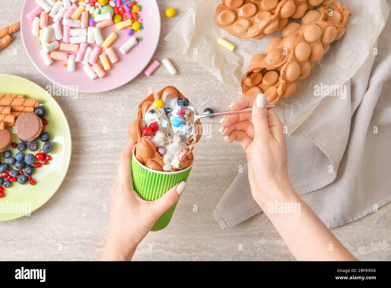 Woman eating sweet bubble waffle at table, top view Stock Photo - Alamy