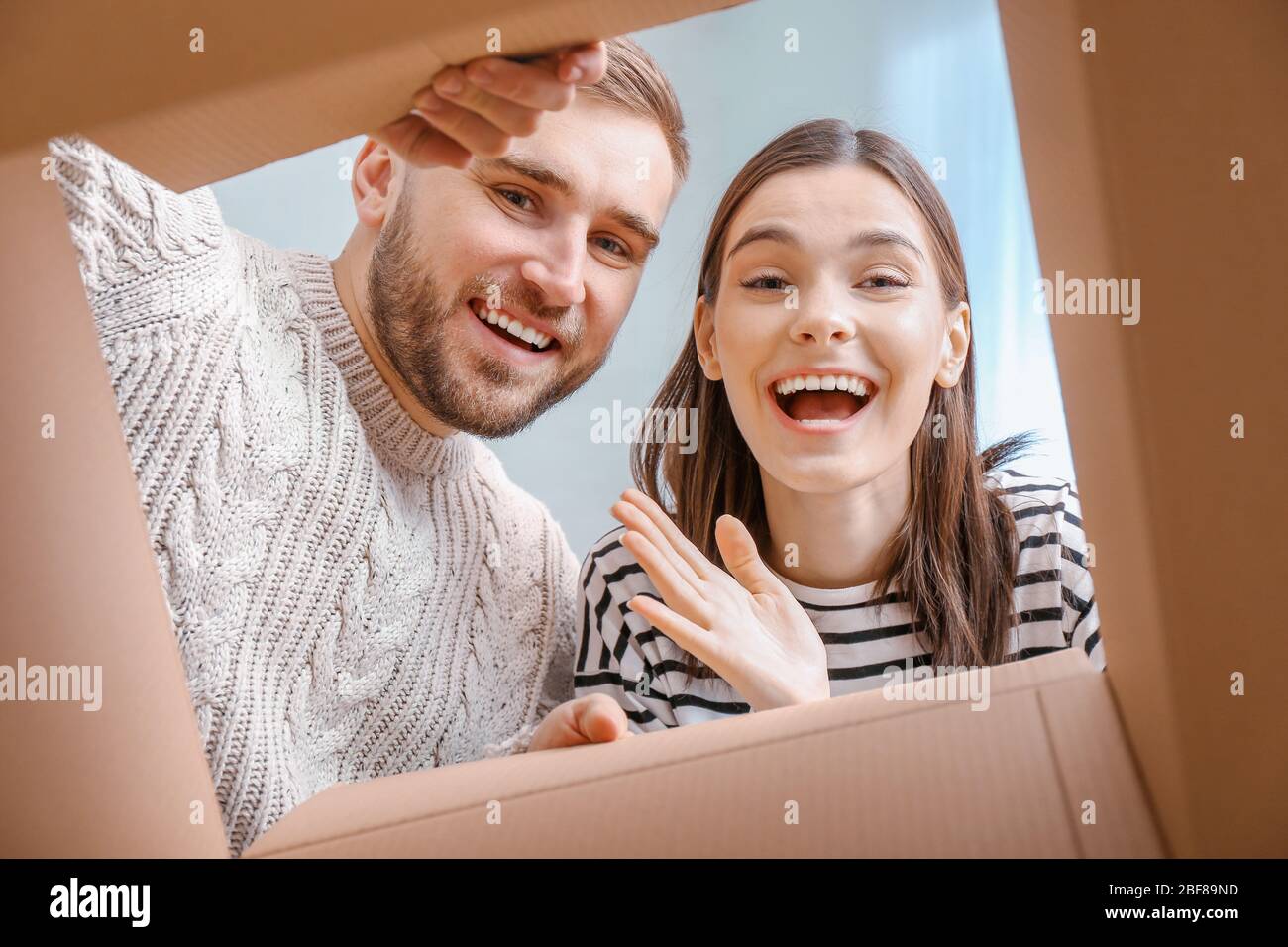 Young couple looking inside cardboard box, bottom view Stock Photo - Alamy