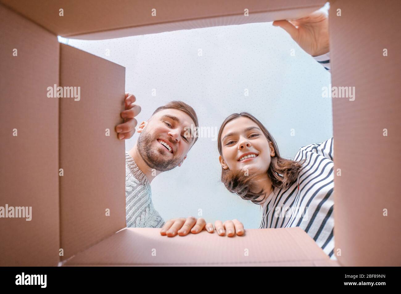 Young couple looking inside cardboard box, bottom view Stock Photo - Alamy