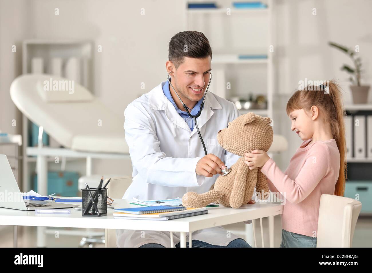 Pediatrician with toy showing little girl how to use stethoscope in ...