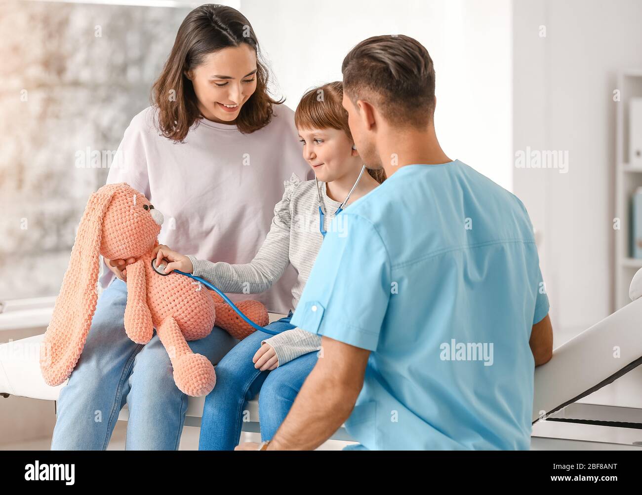 Pediatrician with toy showing little girl how to use stethoscope in ...