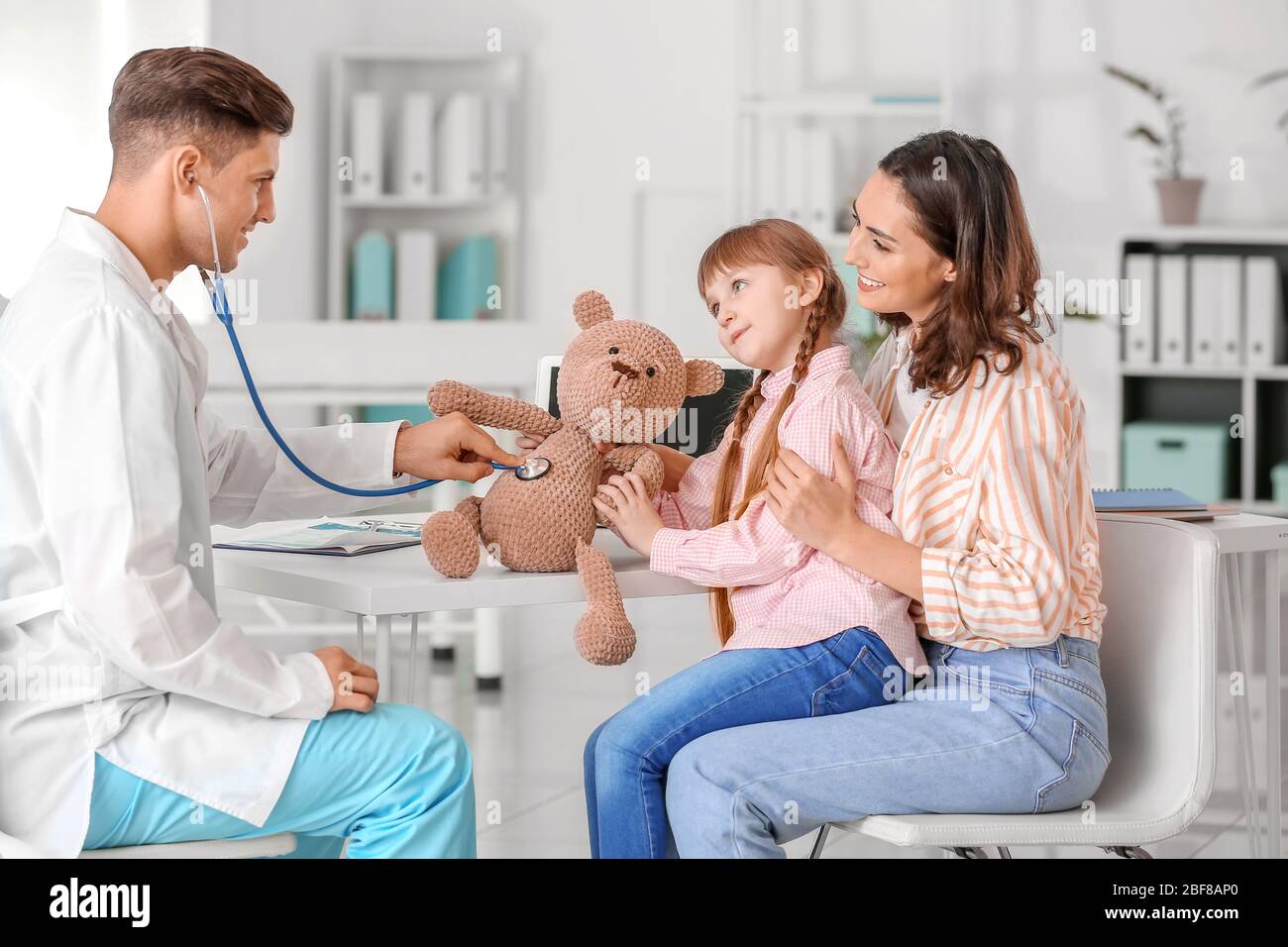 Pediatrician with toy showing little girl how to use stethoscope in ...