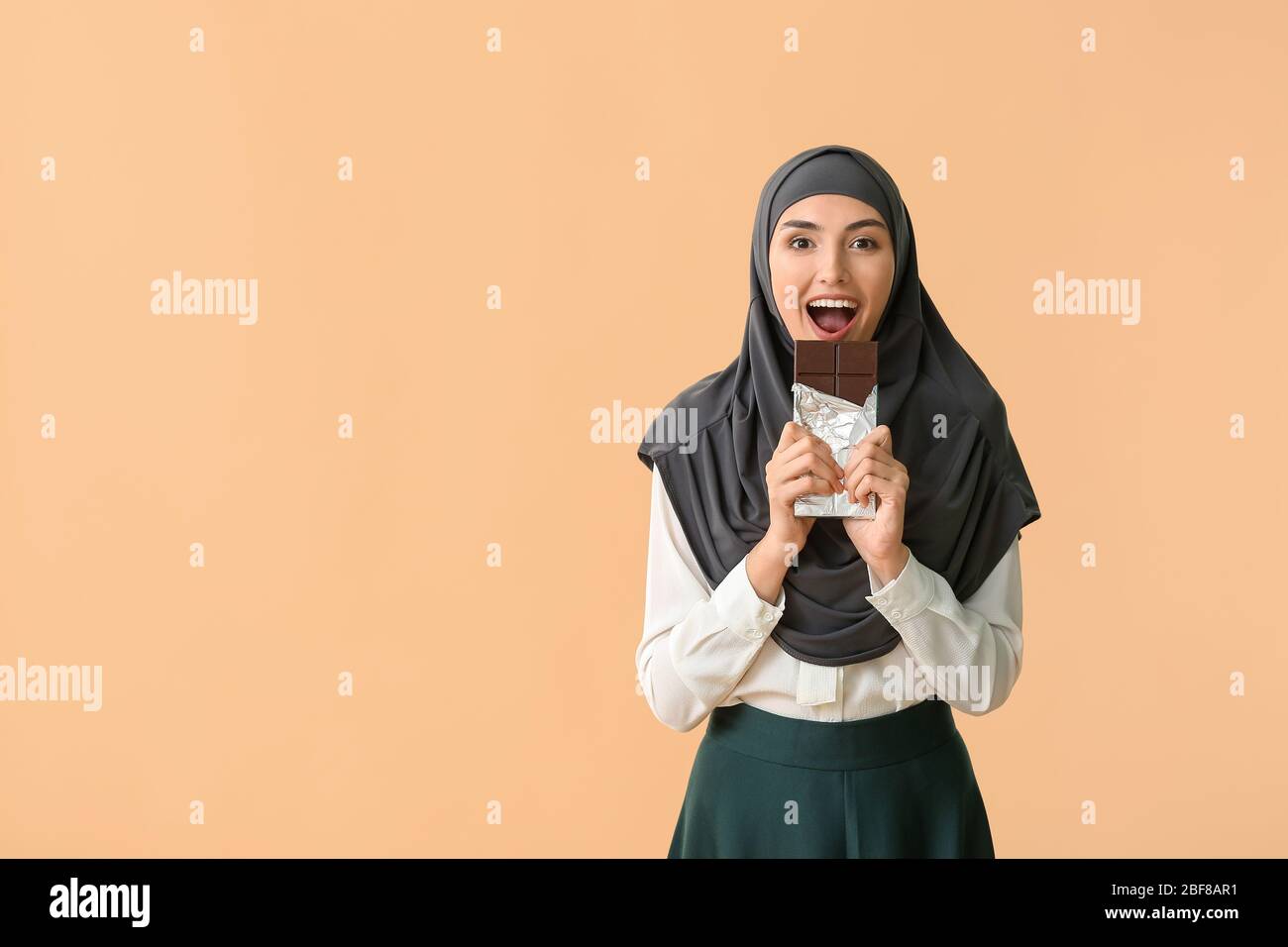 Beautiful Muslim woman eating tasty chocolate on color background Stock ...