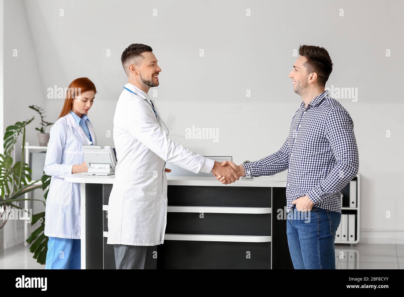 Male doctor and patient shaking hands in clinic Stock Photo - Alamy