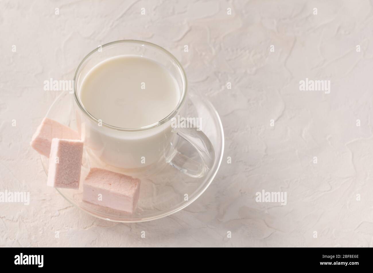 Milk in a transparent cup with saucer and pastille on a light ...