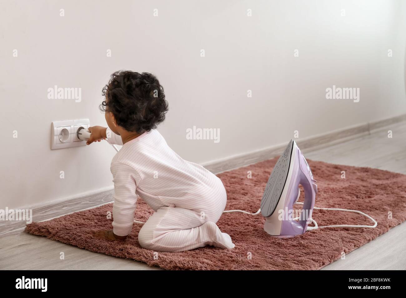 Little African-American baby playing with socket and iron at home ...