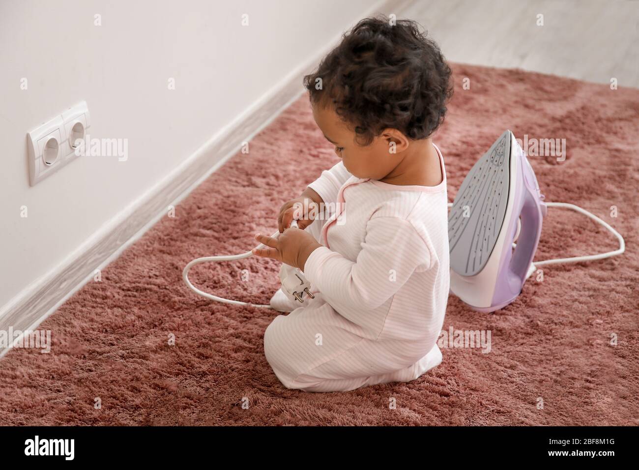 Little African-American baby playing with socket and iron at home ...