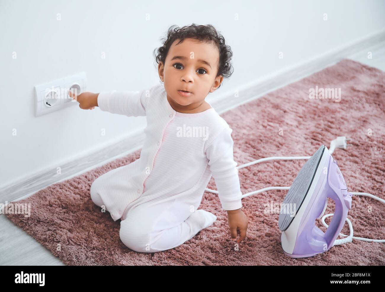 Little African-American baby playing with socket and iron at home ...
