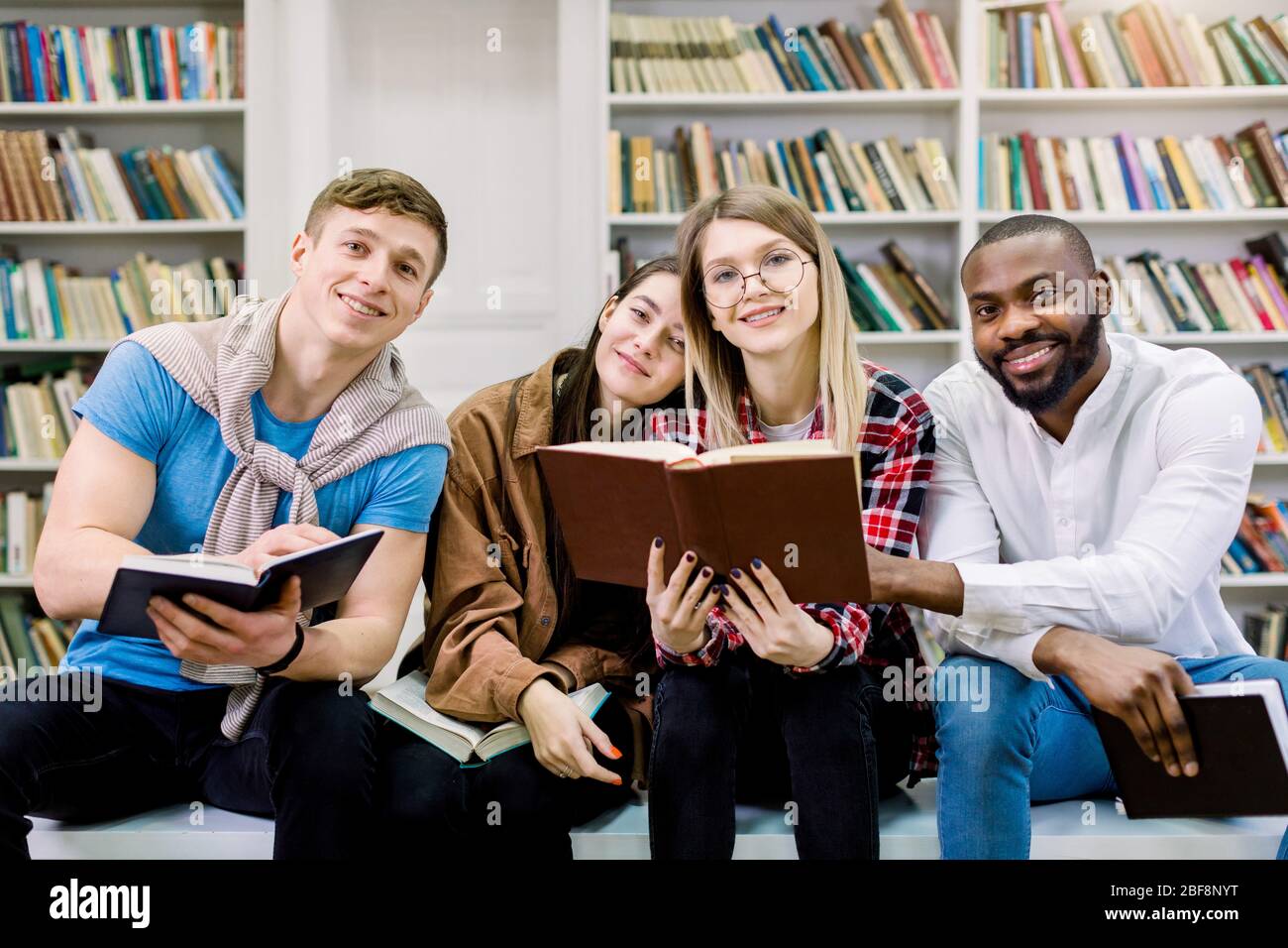 Four multiethnic cheerful students friends in the library, reading ...