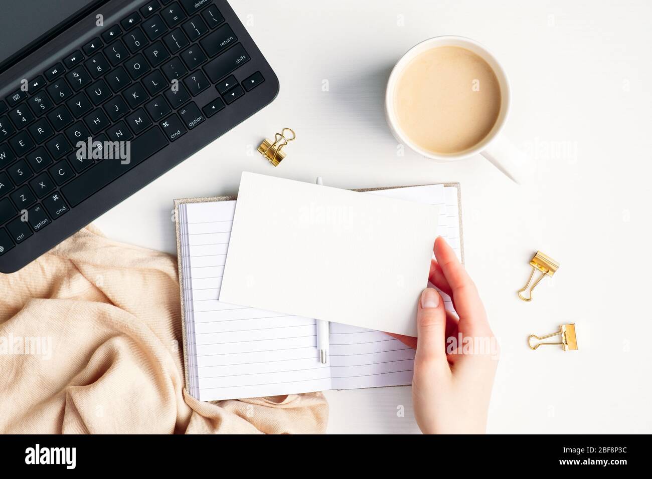 Female workspace with cup of coffee, hand holding blank paper card ...