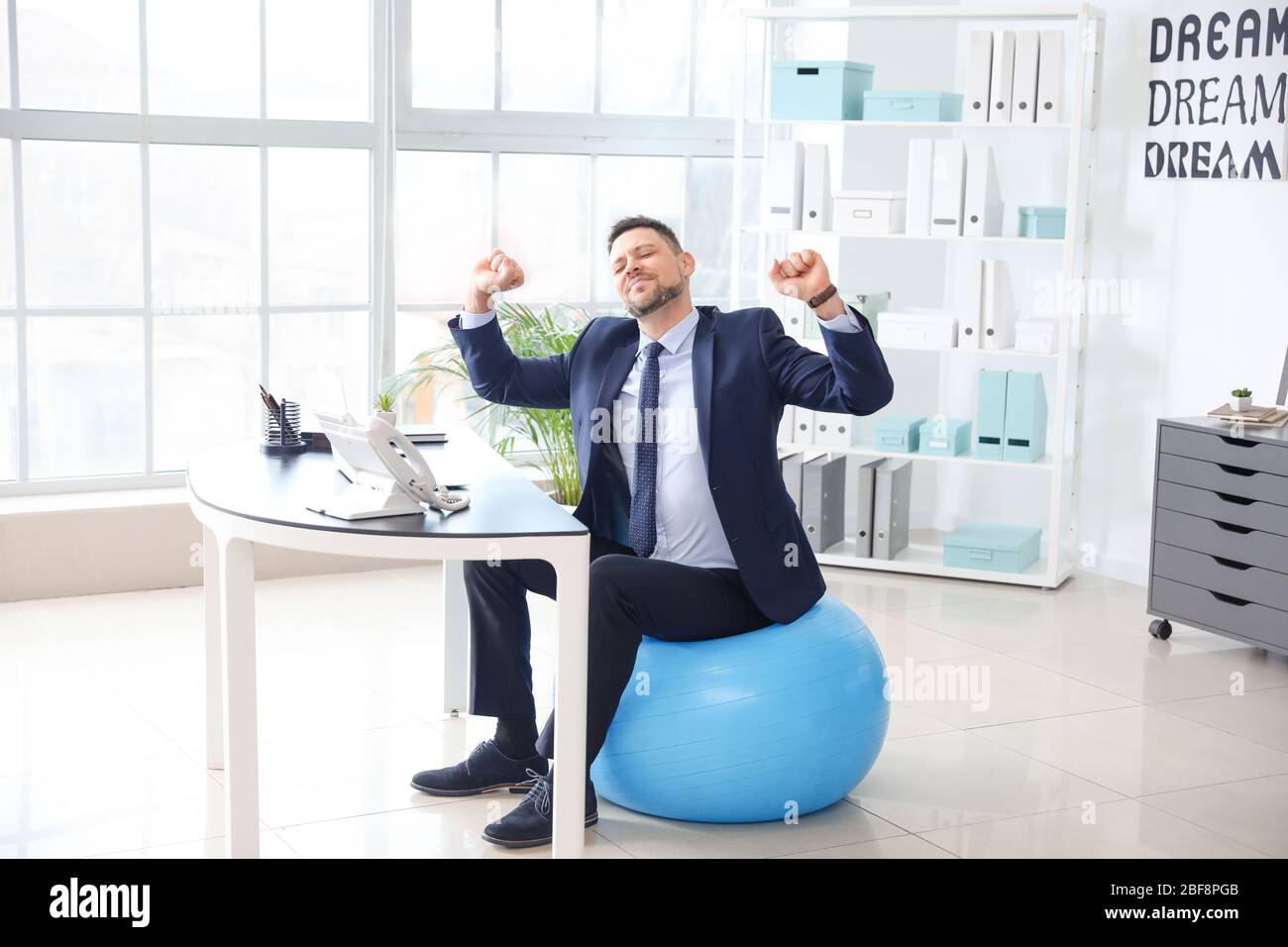 Businessman sitting on fitness ball while working in office Stock Photo ...