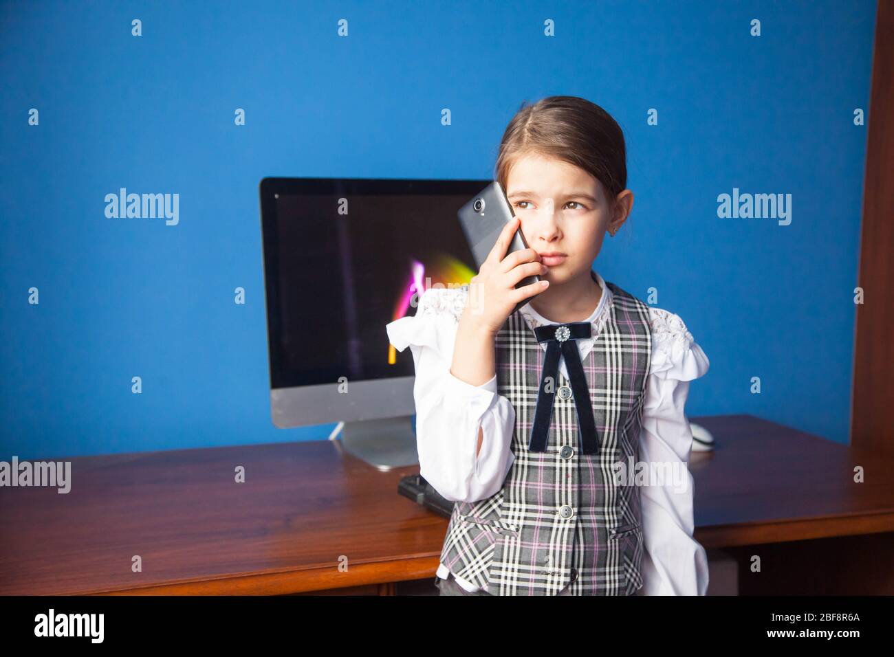 a girl in a business suit stands at the computer and talks on the phone ...