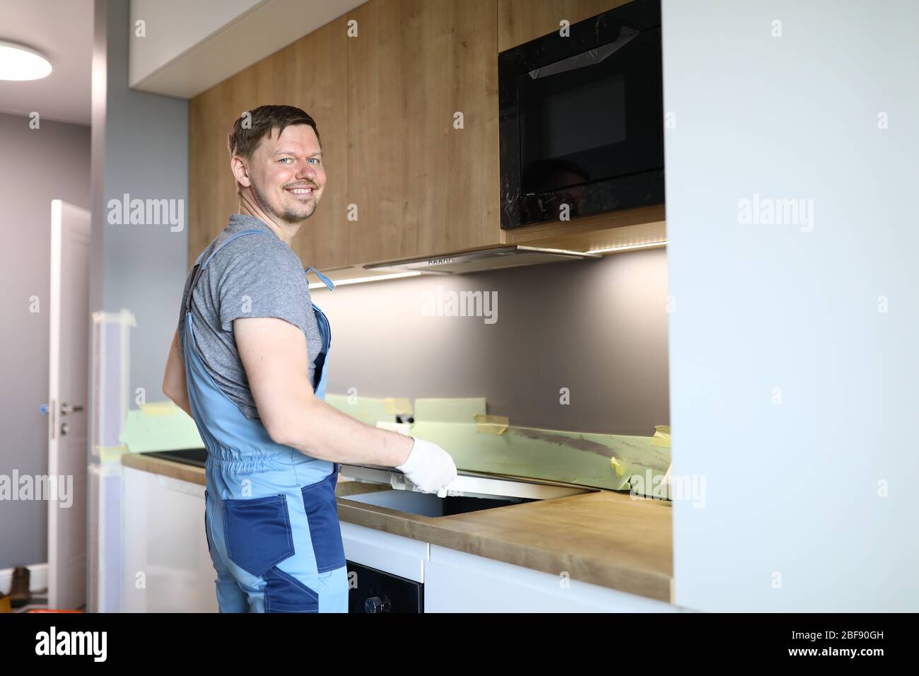 Happy man in work clothes sets hob in kitchen Stock Photo - Alamy