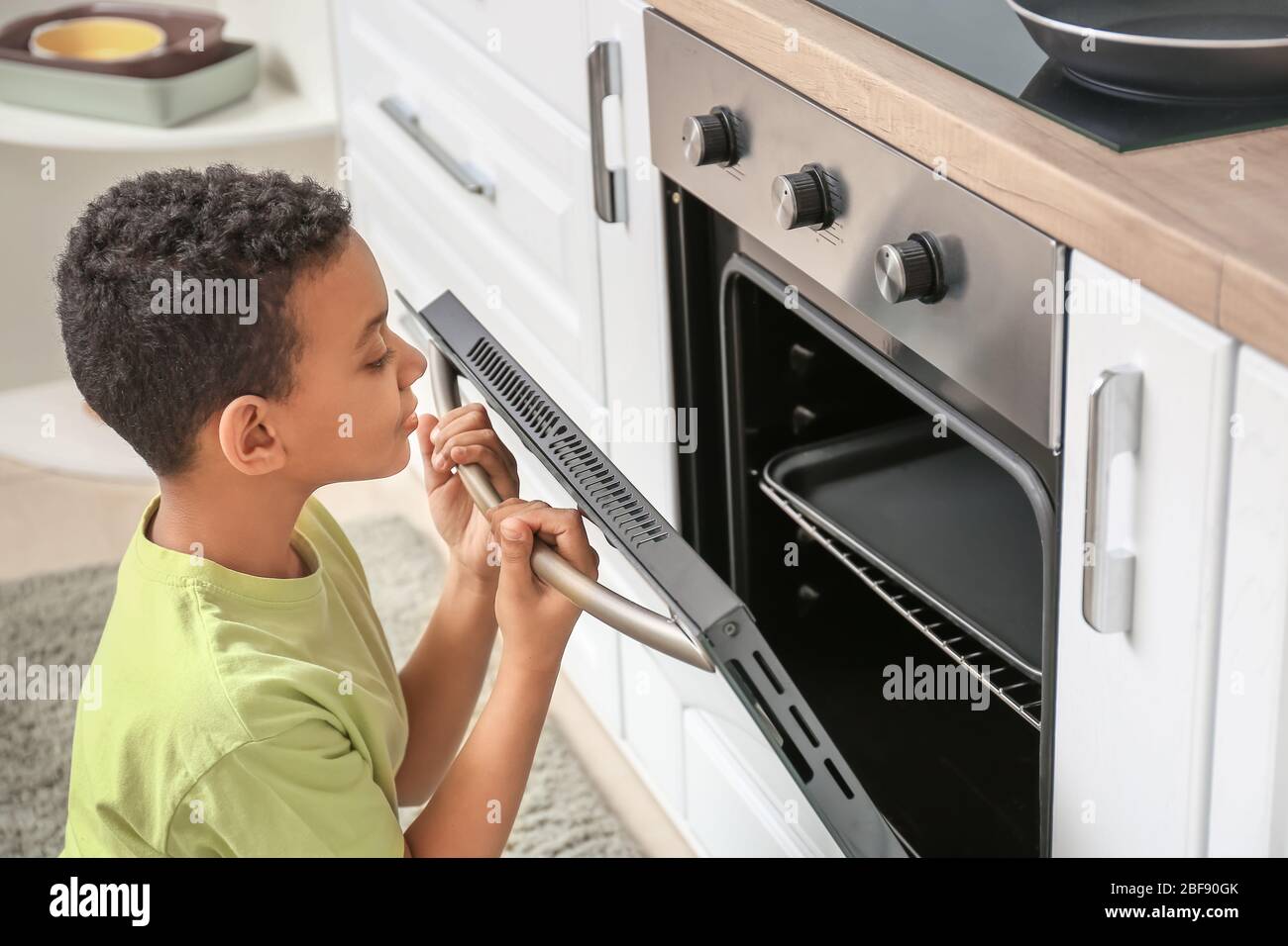 Little African-American boy playing with oven in kitchen. Child in ...