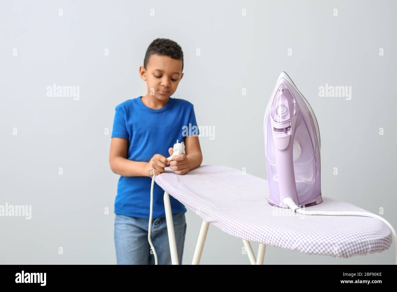 Little African-American boy playing with iron on light background ...