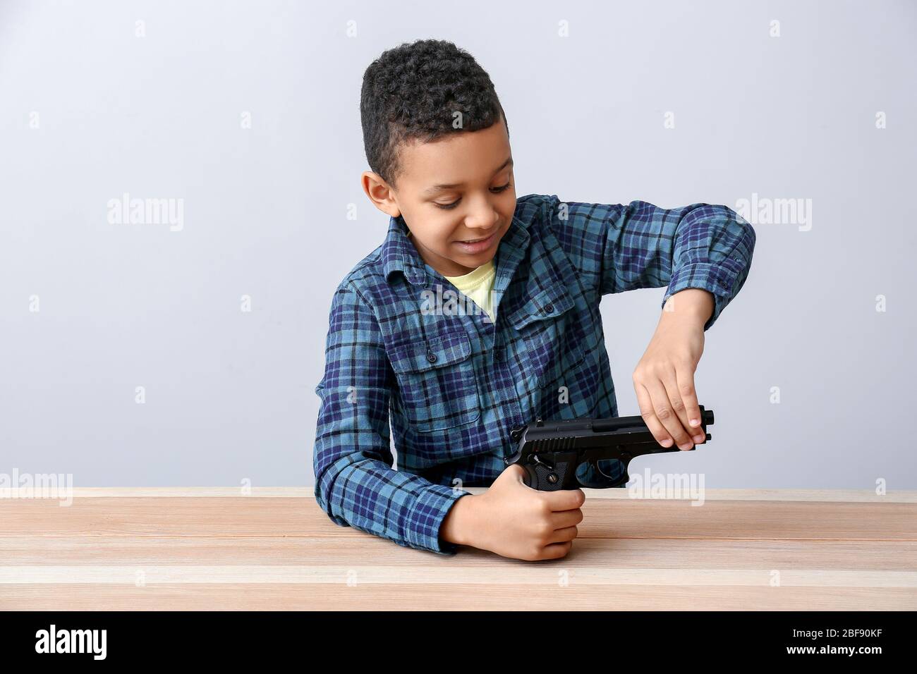 Little African-American boy playing with gun at table. Child in danger ...