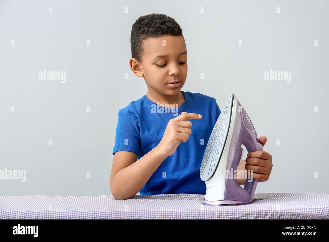 Little African-American boy playing with iron on light background ...
