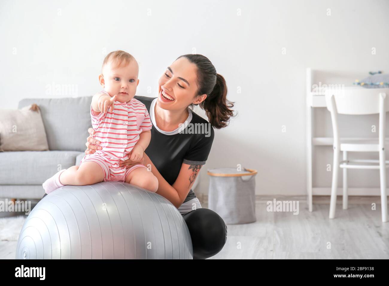 Young sporty mother and her baby doing exercises with fitball at home ...
